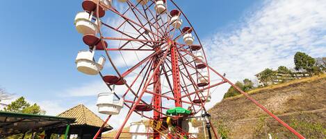 Uma grande roda gigante com cabines, uma estrutura coberta e uma colina ao fundo.