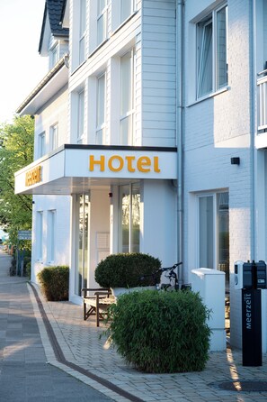 Um hotel com fachada branca, entrada visível e uma placa com a inscrição 'HOTEL'.
