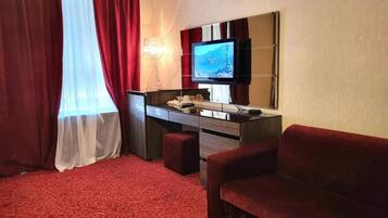 Quarto de hotel com tapete vermelho, escrivaninha com computador, televisão e sofá vermelho.