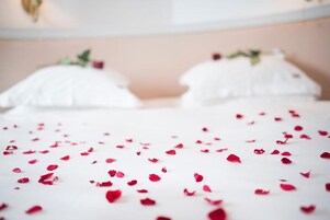 Uma cama com roupa de cama branca e pétalas de rosa vermelha espalhadas.