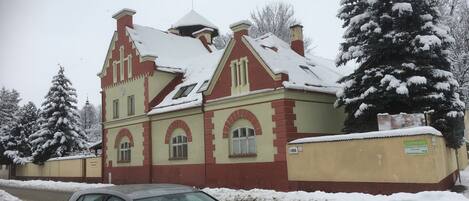 Um edifício com fachada vermelha e bege, janelas em arco e telhado coberto de neve.