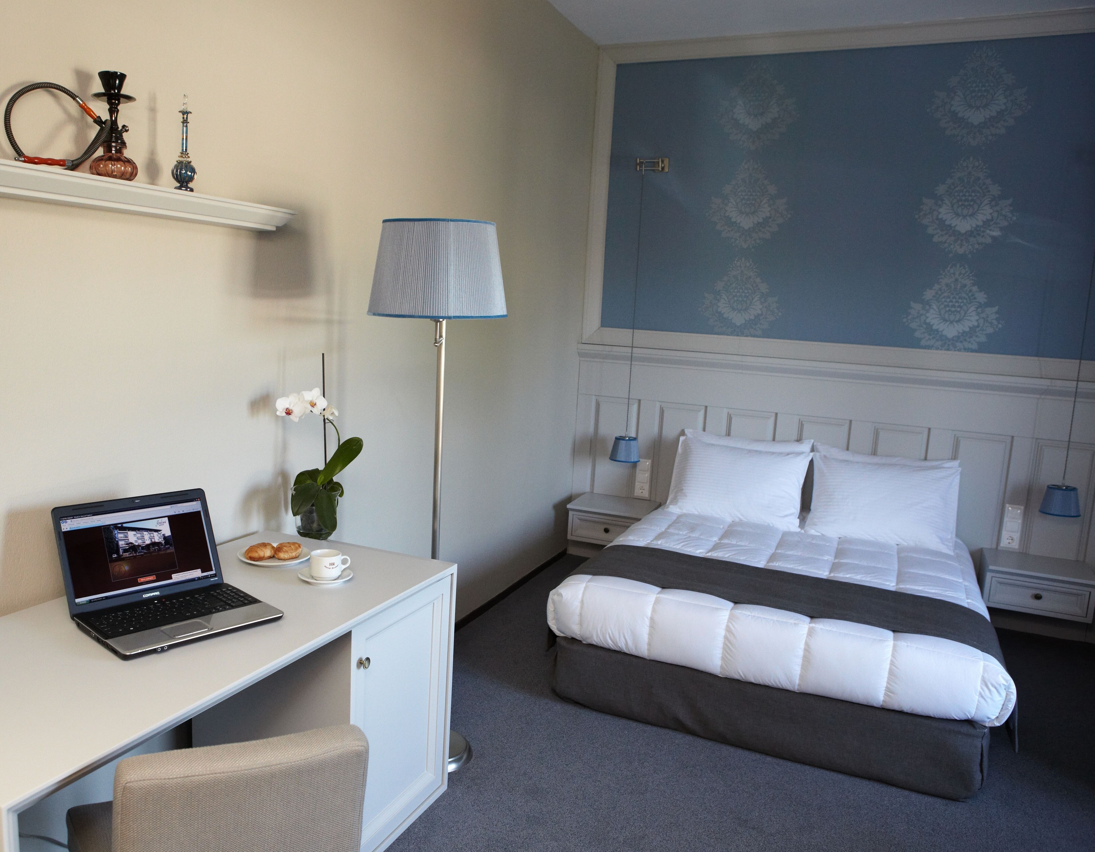 Quarto de hotel com cama, escrivaninha, computador portátil e luminária.