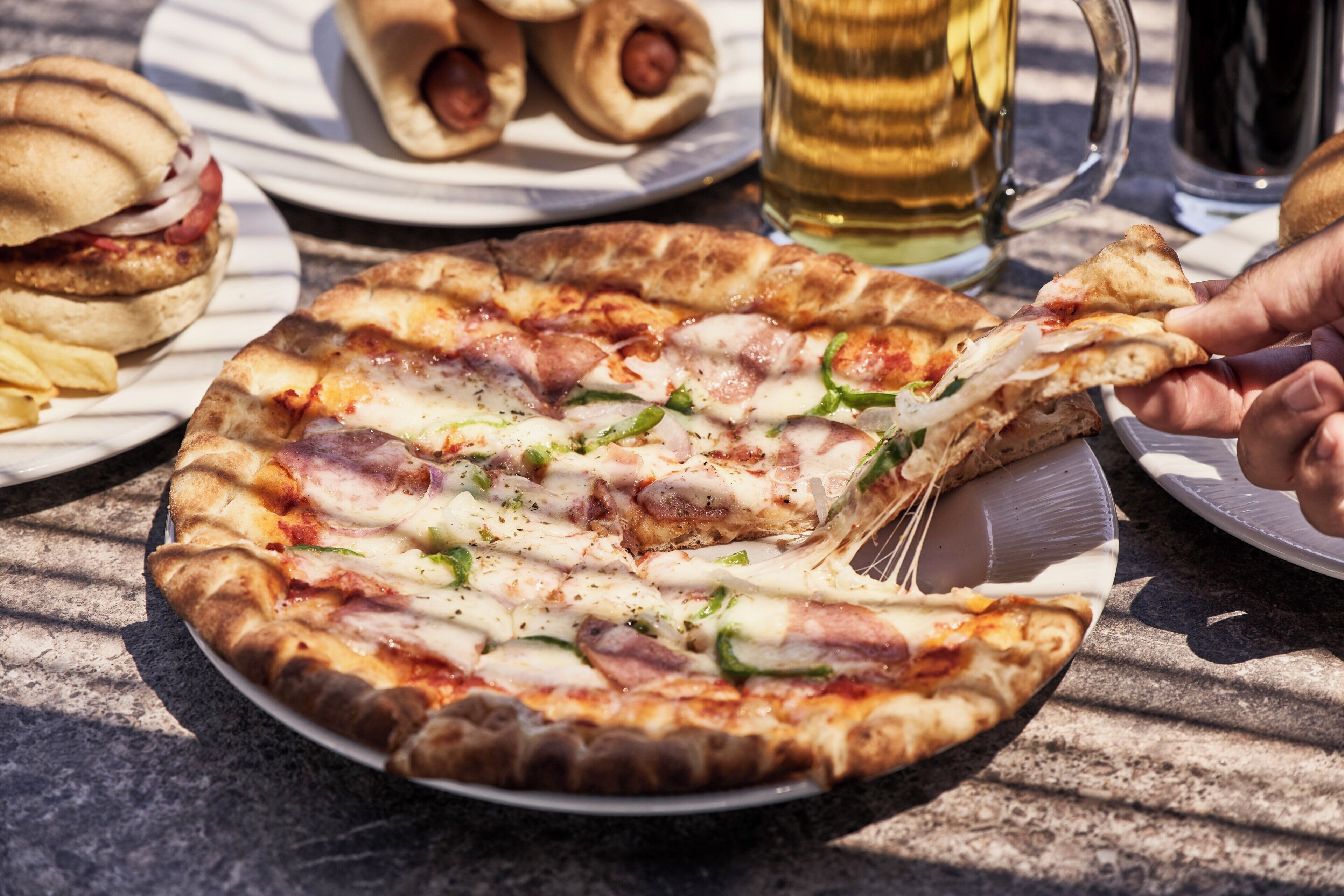Uma pizza com queijo, presunto e pimentões verdes em um prato.