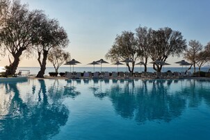 Piscina com espreguiçadeiras e guarda-sóis, árvores e céu claro.