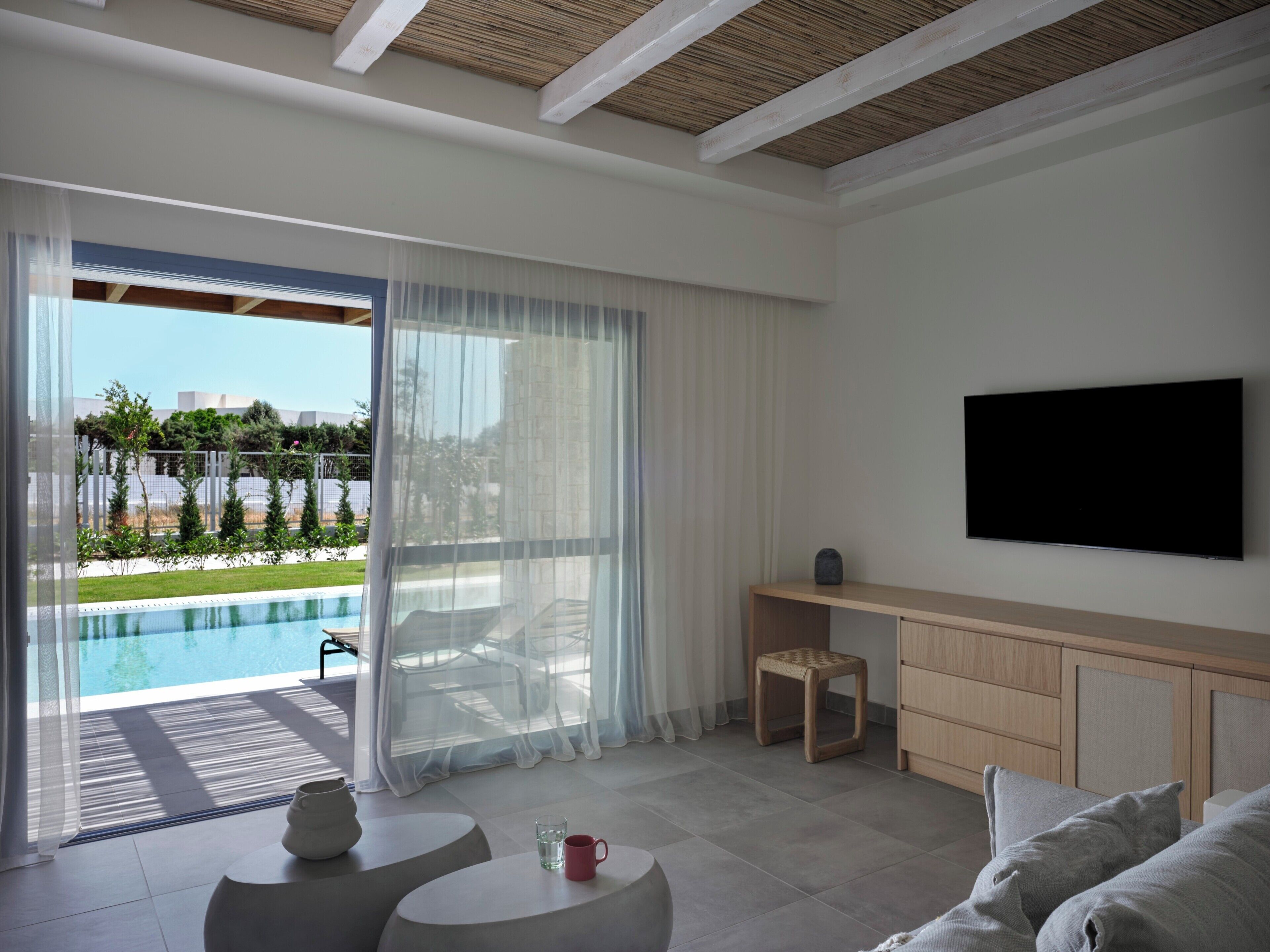 Uma sala de estar moderna com televisão de tela plana, vista para a piscina e porta de vidro deslizante.