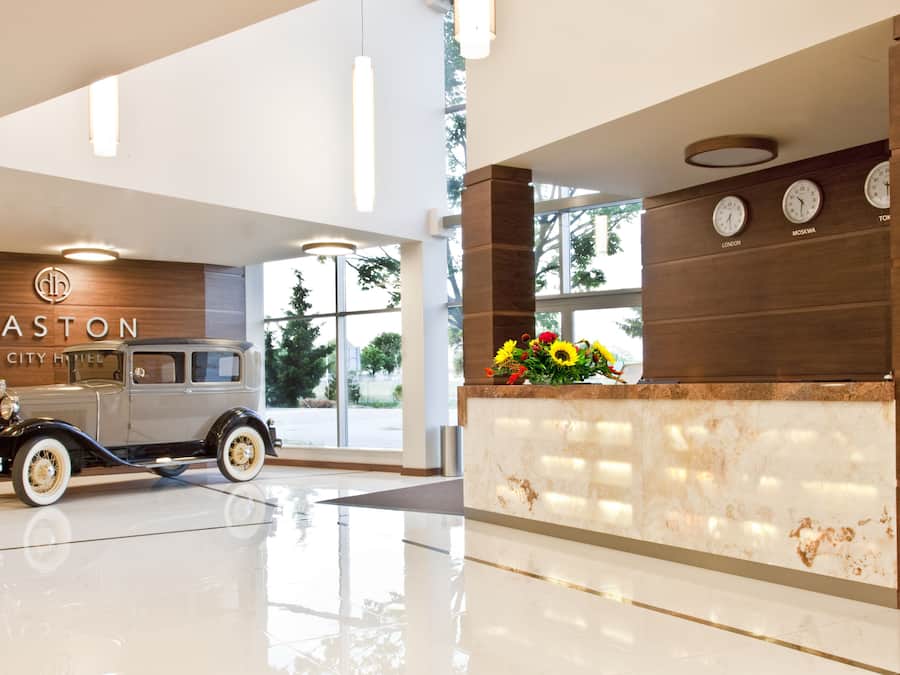Um saguão de hotel moderno com um carro antigo, um balcão de recepção e relógios mostrando diferentes fusos horários.