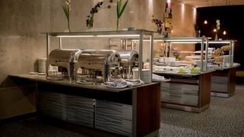 Disposição de buffet com estação de café, vitrines de vidro e decorações florais.