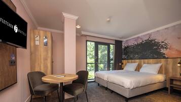 Quarto de hotel com cama, duas cadeiras, uma mesa pequena, televisão e uma janela grande.