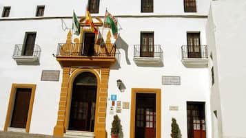 Um edifício branco com um arco central, várias varandas e bandeiras.