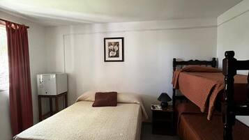 Uma cama de solteiro com cabeceira, mesa de cabeceira com abajur, quadro na parede e janela com cortinas.