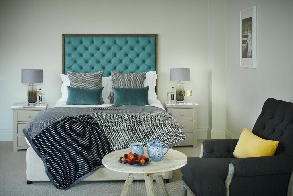 Quarto com uma cama grande, duas mesas de cabeceira, uma mesa redonda com frutas e uma poltrona preta.