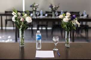 Uma mesa de conferência com vasos de flores, uma garrafa de água e uma taça de vinho.