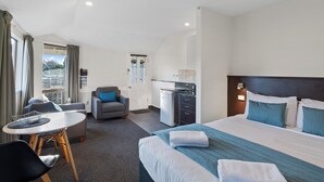Quarto de hotel com cama, escrivaninha, cadeira, sofá, cozinha compacta e vista para o exterior.