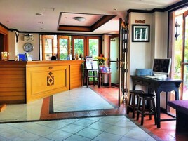 Uma área de recepção com balcão de madeira, uma mesa com computador e uma cadeira.