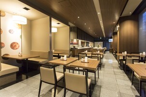 Restaurante moderno com várias mesas e cadeiras, área de cozinha ao fundo e interior limpo e bem iluminado.
