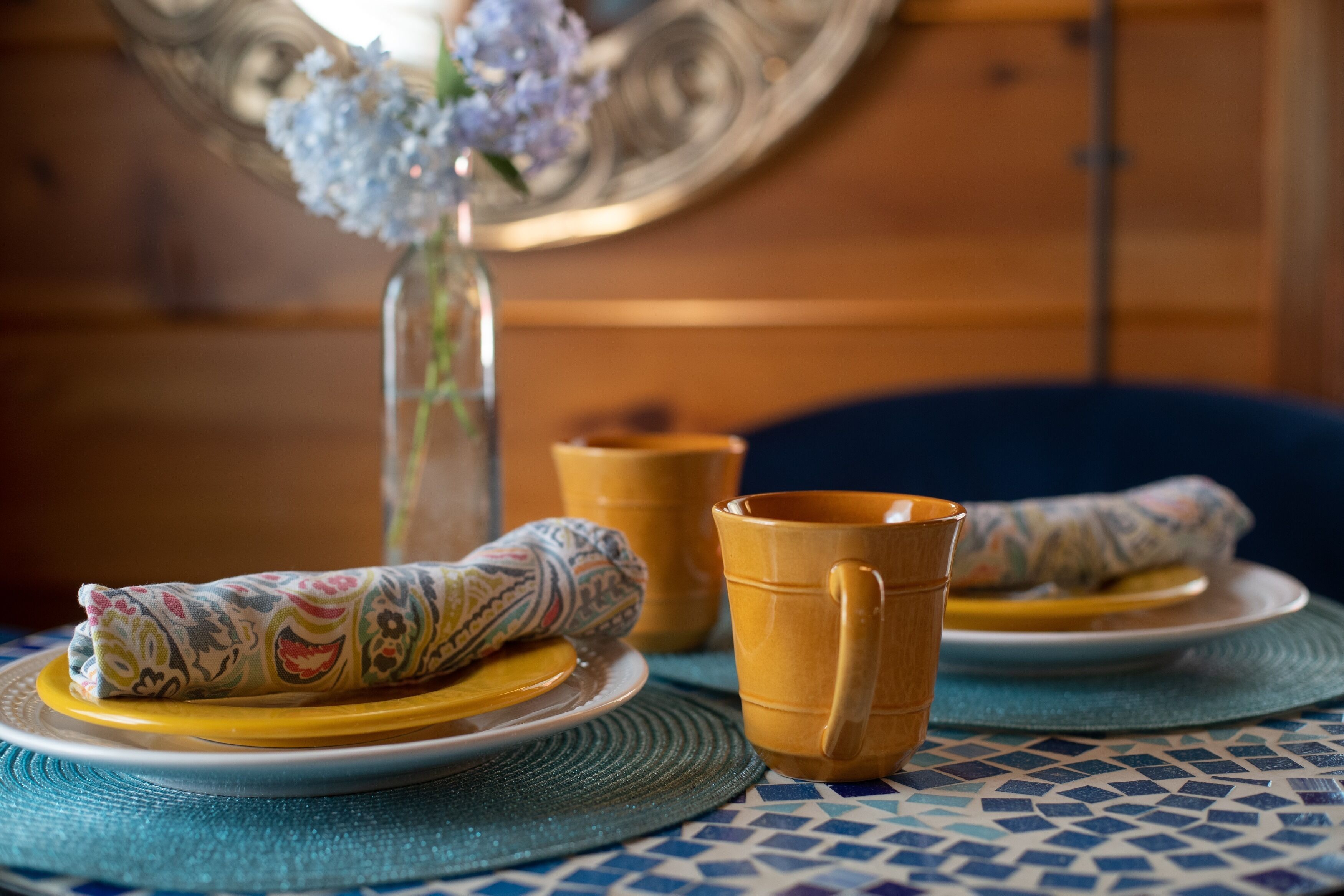 Uma mesa com toalha estampada, um vaso com flores e duas xícaras de cerâmica amarelas.