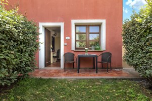 Um pátio com duas cadeiras, uma mesa, uma porta e uma janela com vista para árvores.