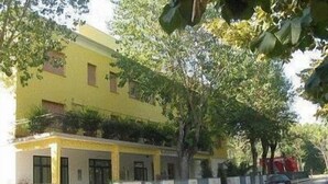 Um edifício amarelo com varanda, portão e um carro estacionado em frente.