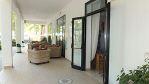 Um corredor com mobiliário de vime, piso de azulejos e uma porta de vidro que dá para um quarto.