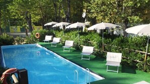 Piscina com trampolim, rodeada por espreguiçadeiras e guarda-sóis brancos.