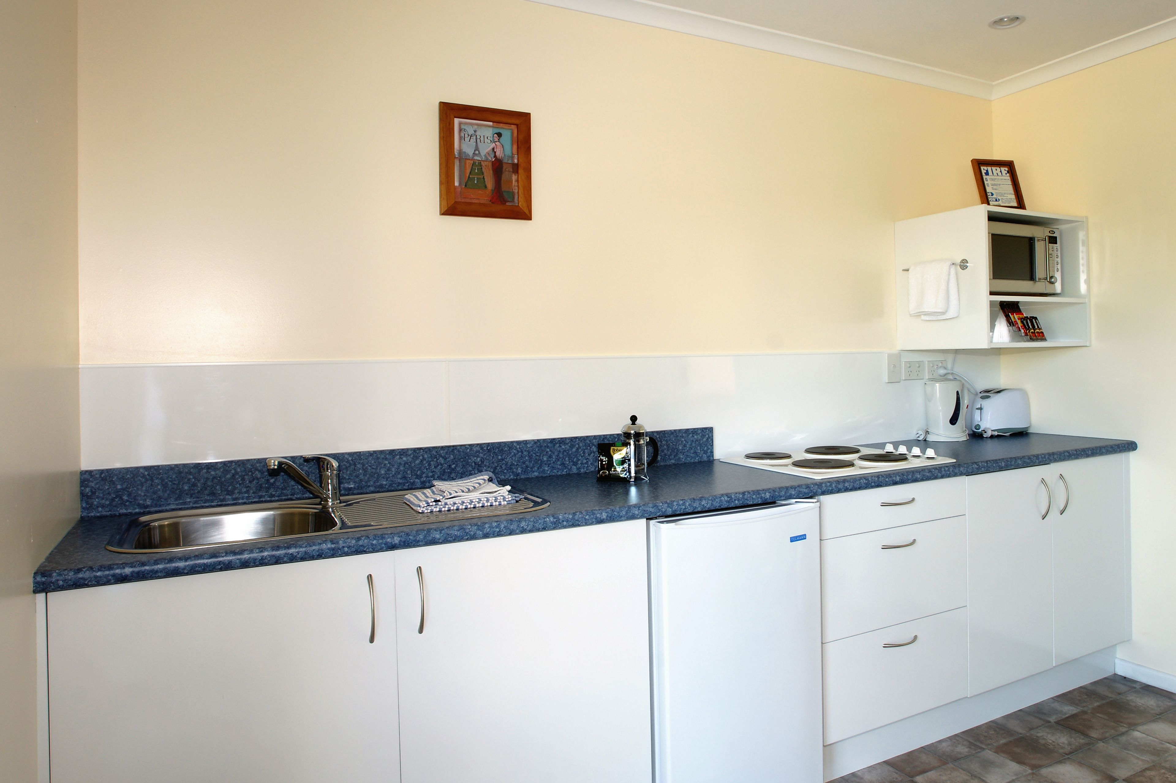 Cozinha com bancada azul, pia de aço inoxidável, armários brancos, micro-ondas e cafeteira.