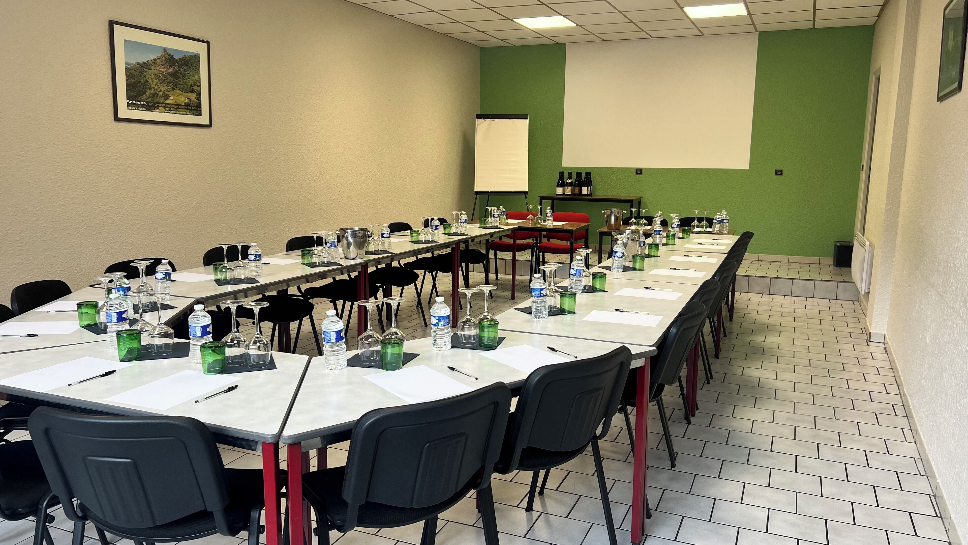 Uma sala de conferências com mesas compridas, cadeiras, garrafas de água e copos de vinho.