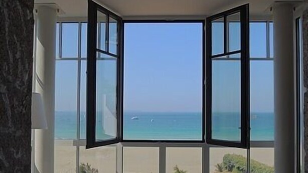 Quarto com uma grande janela saliente com vista para a praia e oceano.