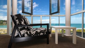 Quarto moderno com uma grande janela com vista para a praia, uma cadeira estampada em preto e branco e uma pequena mesa branca.