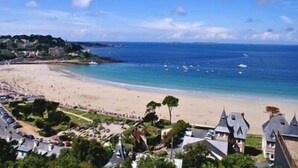 Uma vila costeira com uma praia, casas de telhados inclinados e um céu azul límpido.