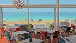 Restaurante com mesas e cadeiras dispostas para frente de uma vista para a praia.
