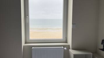 Quarto com uma grande janela com vista para uma praia, um radiador e uma mesinha de cabeceira.