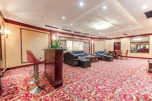 Um quarto amplo com carpete vermelho, área de bar com banquetas, conjunto de sofás e um espelho grande.