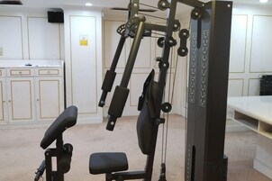 Academia com equipamentos de ginástica, parede branca e carpete bege.