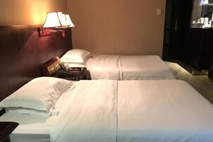 Quarto de hotel com duas camas, uma mesa de cabeceira e uma luminária.
