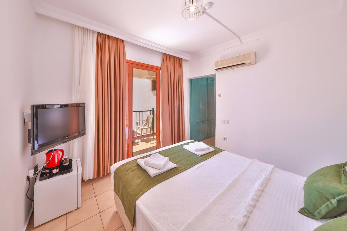 Quarto de hotel com cama, televisão, máquina de café, porta de correr para uma varanda e ar condicionado.