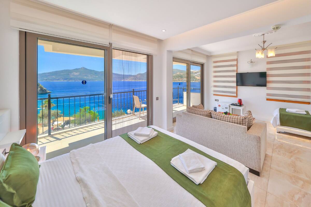 Quarto de hotel com varanda, uma cama, um sofá, televisão e vista para o mar.