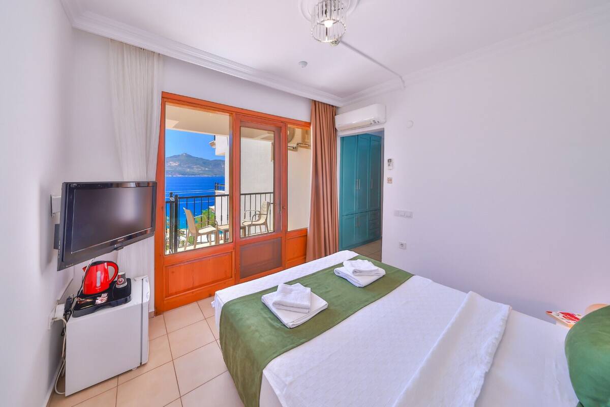 Quarto de hotel com cama, televisão, cafeteira e vista para o mar.