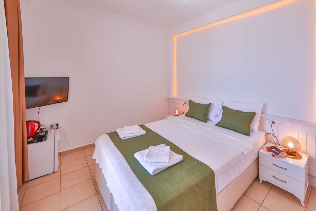 Quarto de hotel bem arrumado com cama, mesas de cabeceira, televisão e máquina de café.