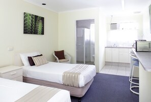 Quarto de hotel com duas camas, um pequeno espaço de estar, uma cozinha compacta e chuveiro.
