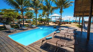 Um deck de madeira com piscina, cadeiras de descanso e guarda-sóis.