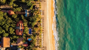 Vista aérea de um resort na praia com várias acomodações tipo bangalô, uma praia de areia e uma vista clara do oceano.