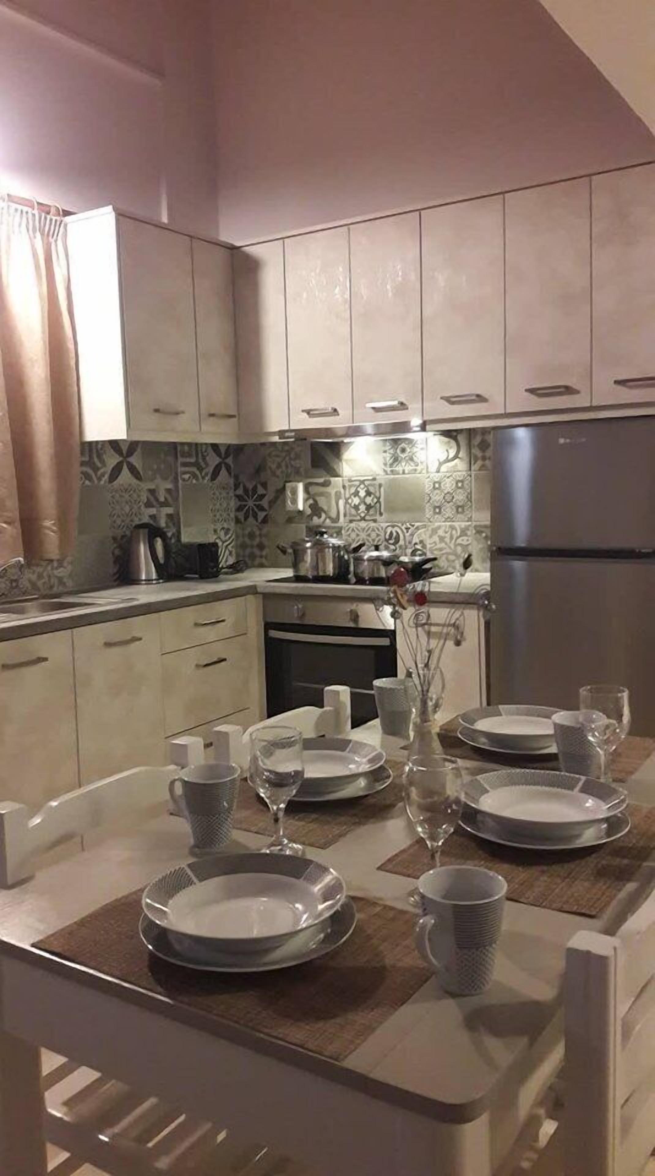 Uma cozinha moderna com armários brancos, uma geladeira de aço inoxidável e uma mesa de jantar posta para quatro pessoas.