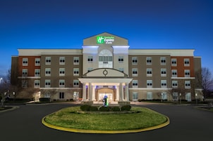 Um hotel Holiday Inn Express & Suites com entrada central, vários andares e um caminho de acesso ajardinado.