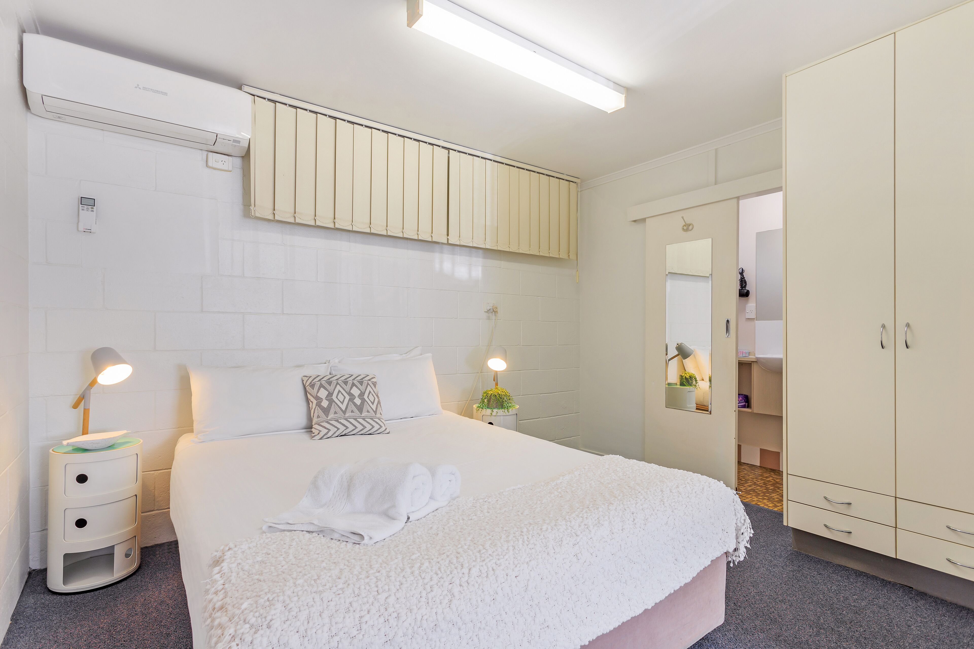 Quarto bem arrumado com uma cama, abajures, guarda-roupa e um espelho.