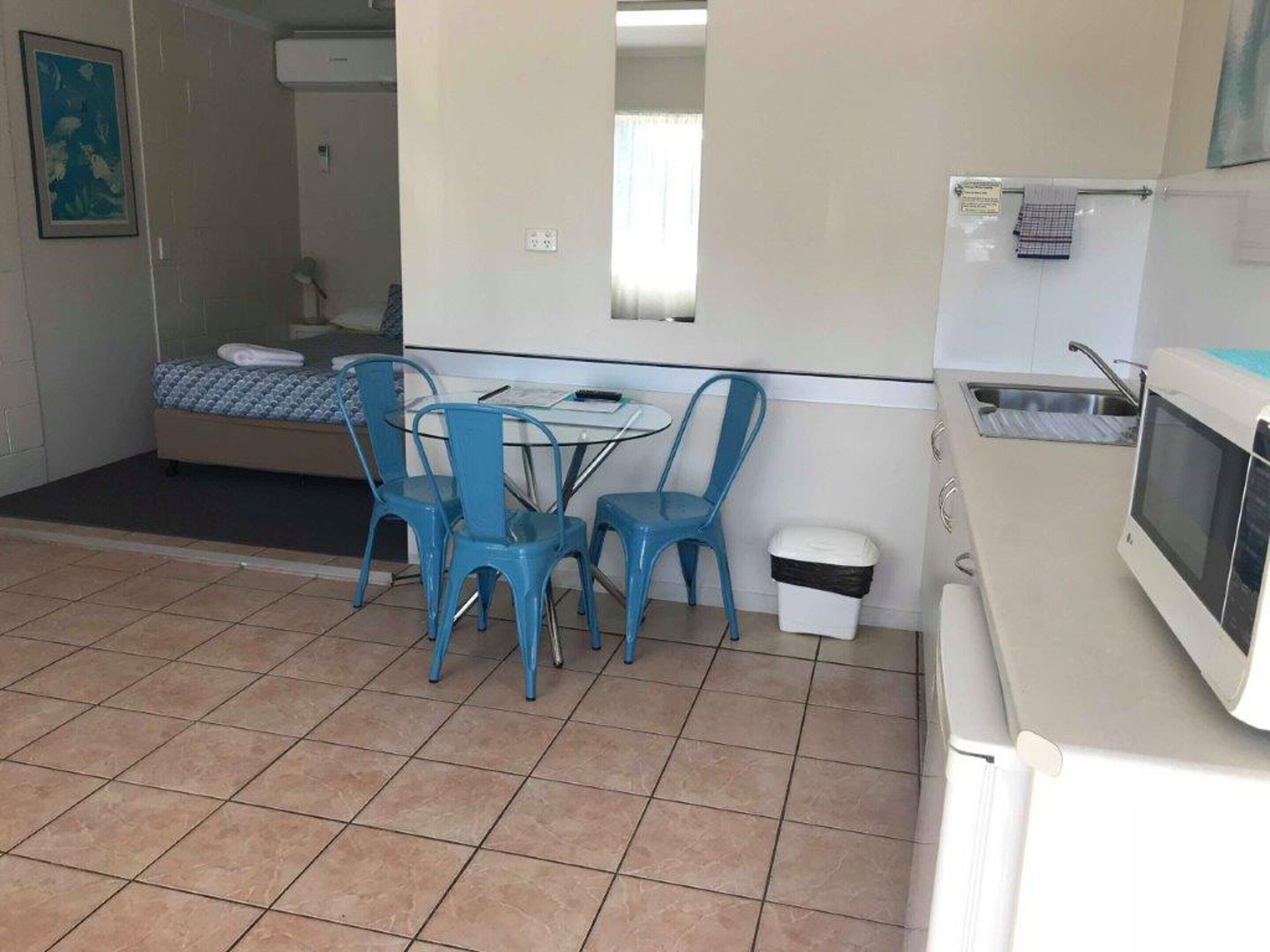 Uma cozinha compacta com micro-ondas, pia e pequena área de refeições com cadeiras azuis.