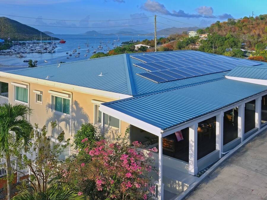 Um edifício moderno com telhado azul, painéis solares e vista para uma marina com barcos.
