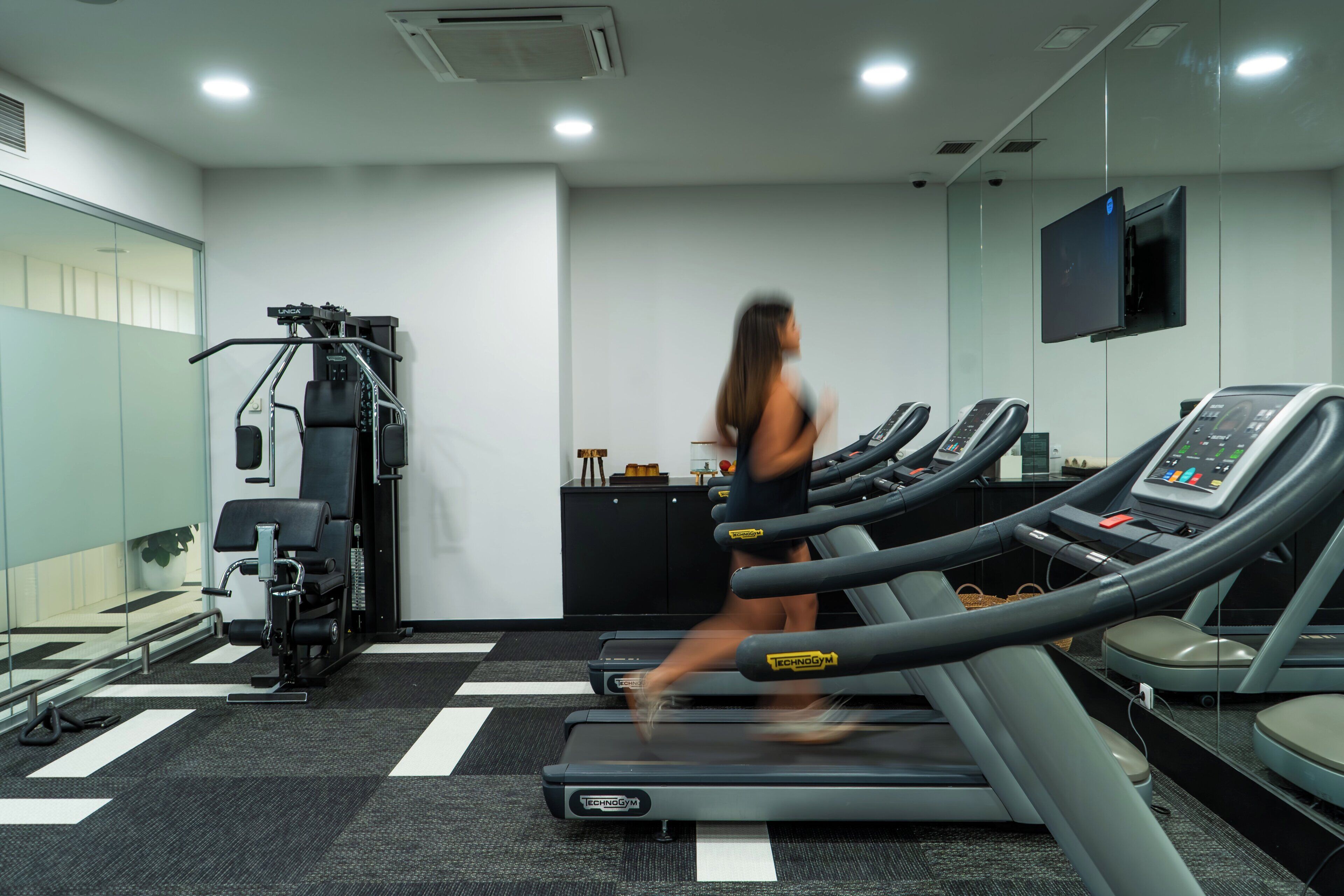 Uma academia com esteiras, aparelhos de musculação e um espelho grande.