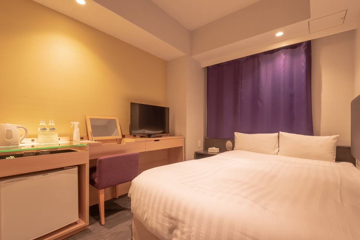 Quarto de hotel com cama, escrivaninha com computador, televisão e minibar.