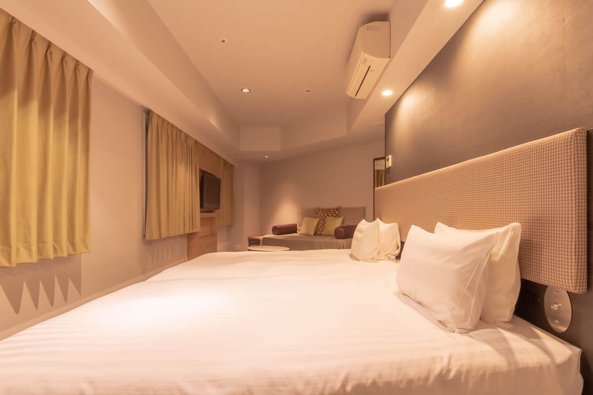 Quarto de hotel com uma cama grande, mesa de cabeceira, ar condicionado fixado na parede e janela com cortinas.