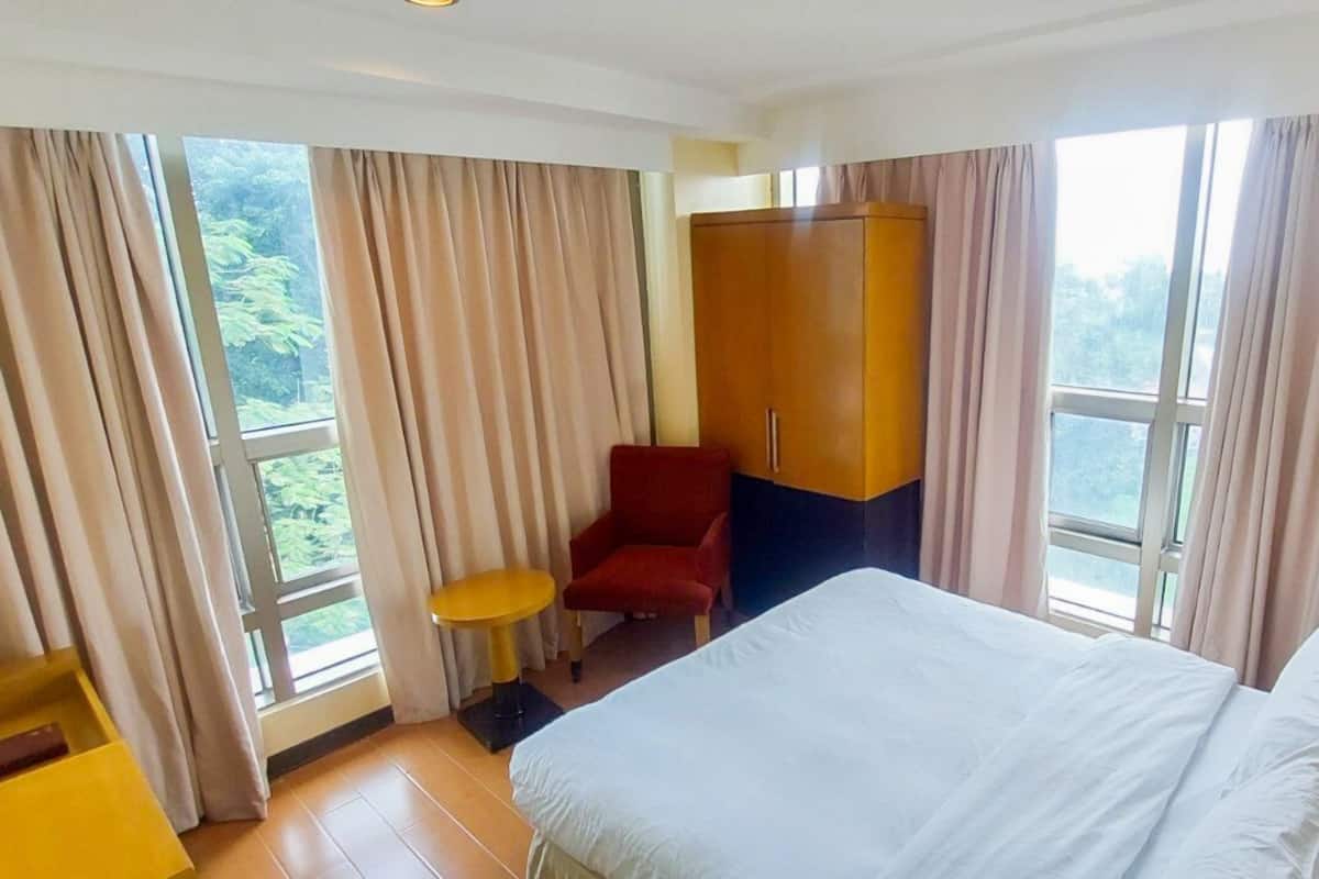 Quarto de hotel com cama, uma cadeira, uma pequena mesa e um guarda-roupa.